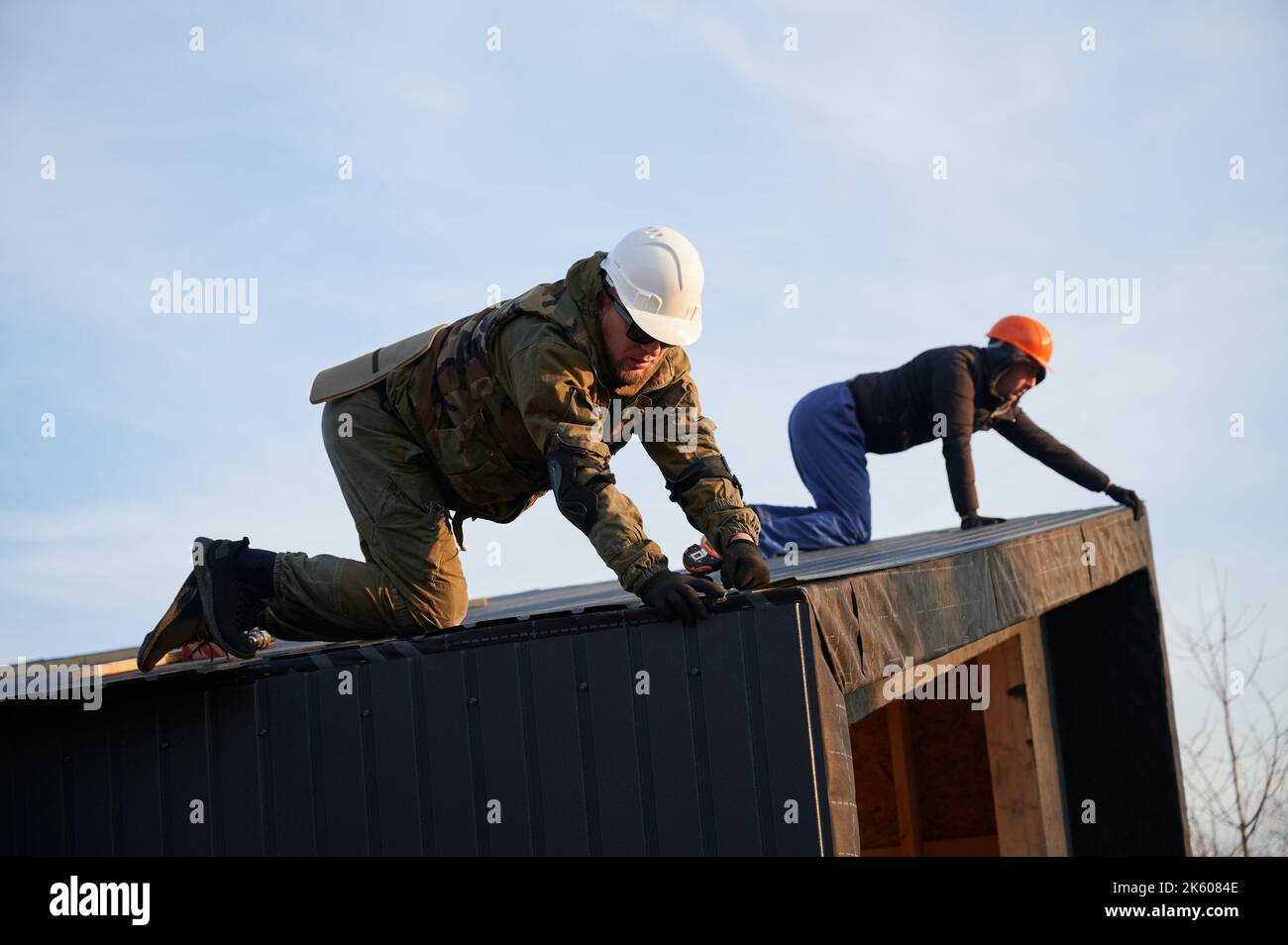 Male builders installing black corrugated iron sheet used as facade of ...