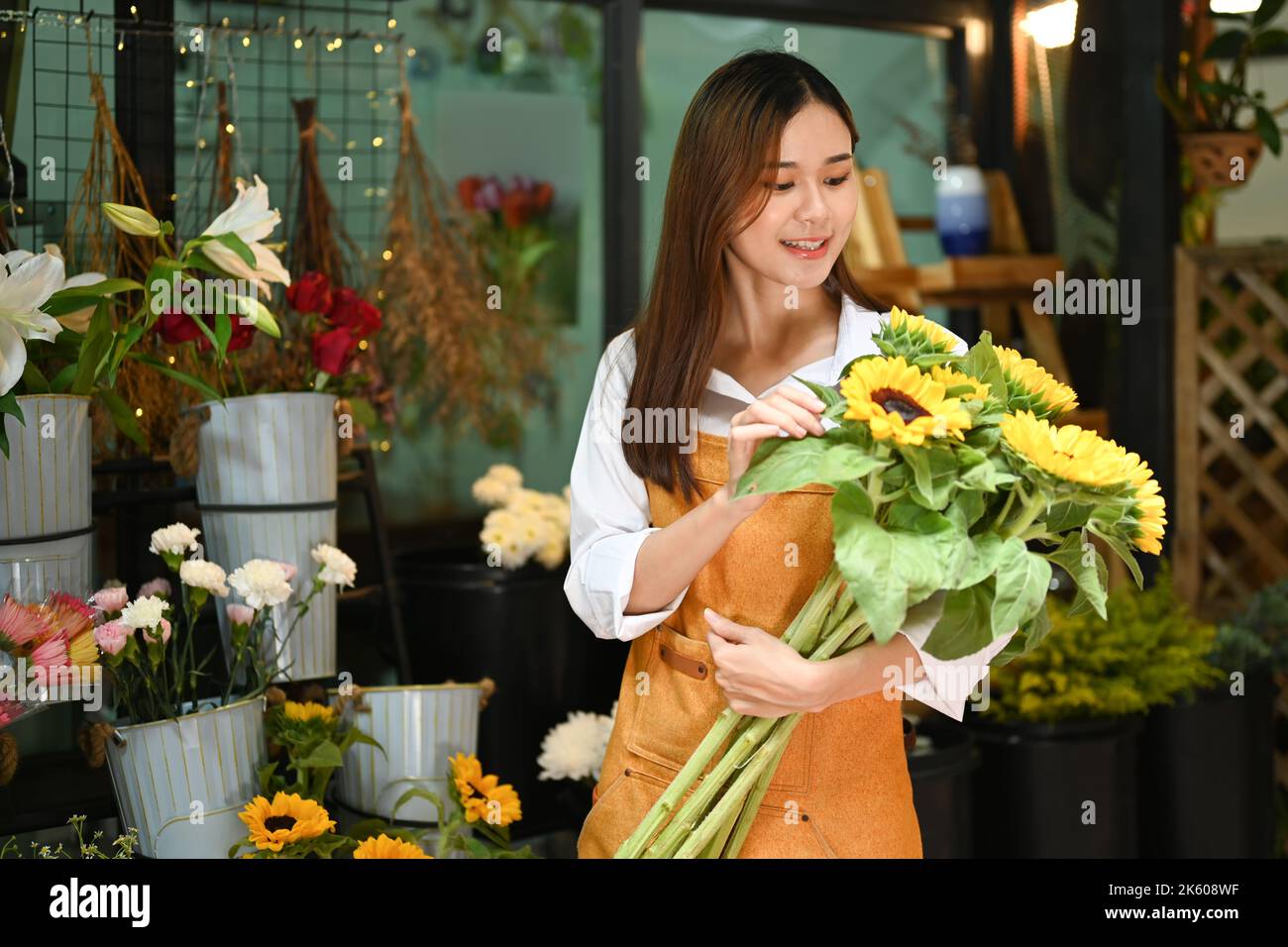 Young woman florist wearing apron holding beautiful sunflowers bouquet ...