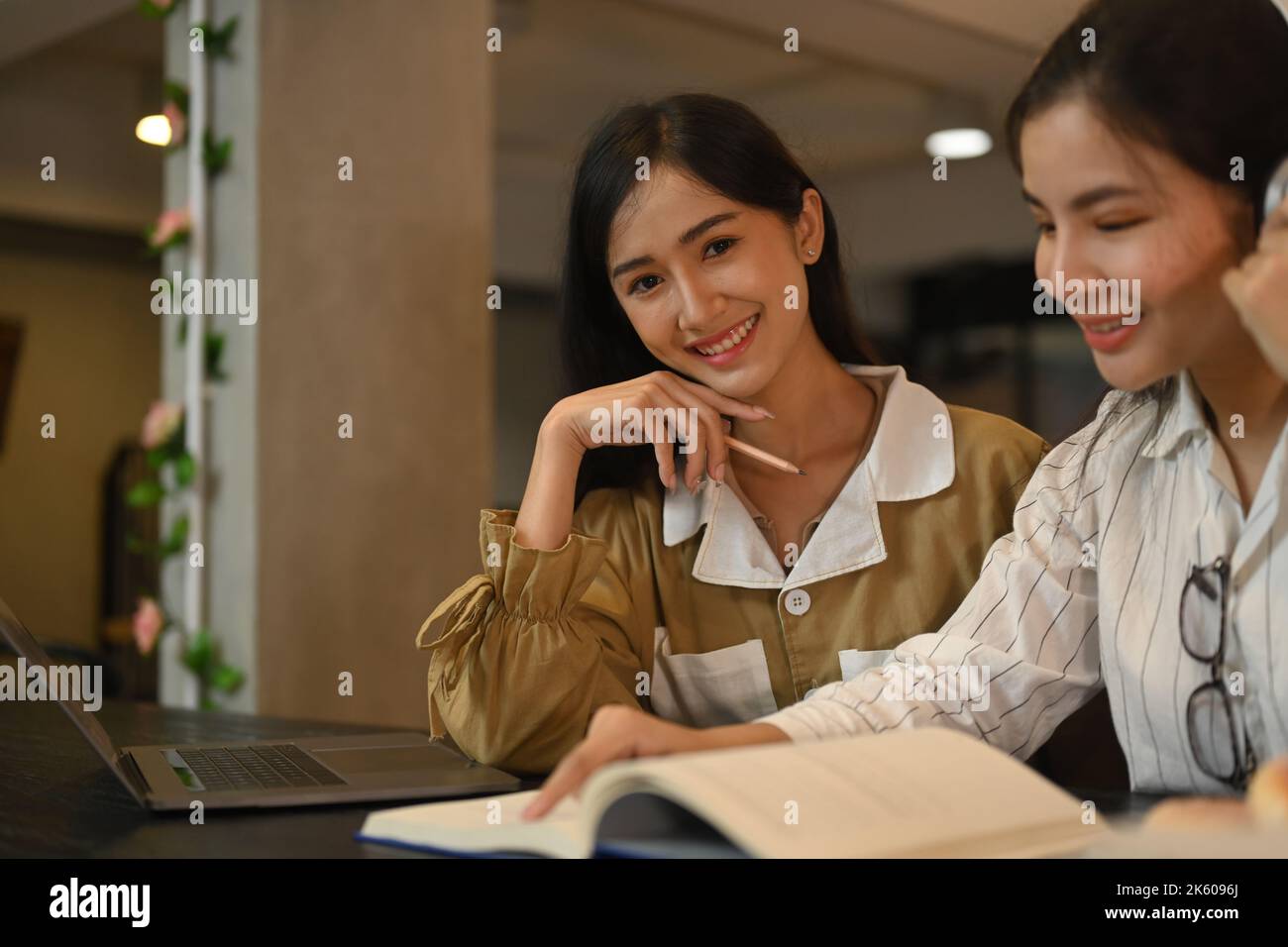 Pretty female students reading book and doing research with her friend ...