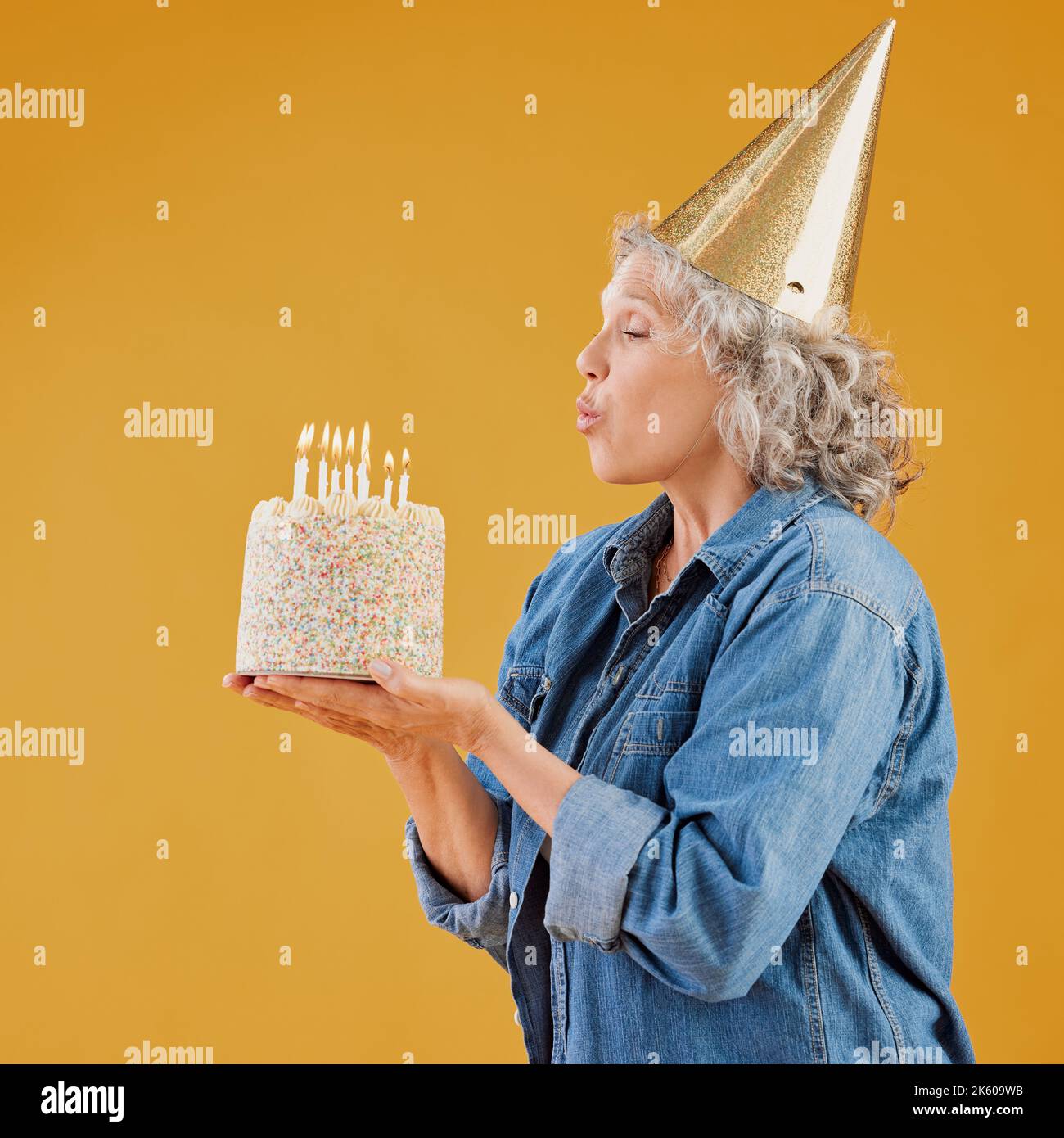 One Happy Mature Caucasian Woman Blowing Out Candles On A Cake She Is Holding While Wearing A