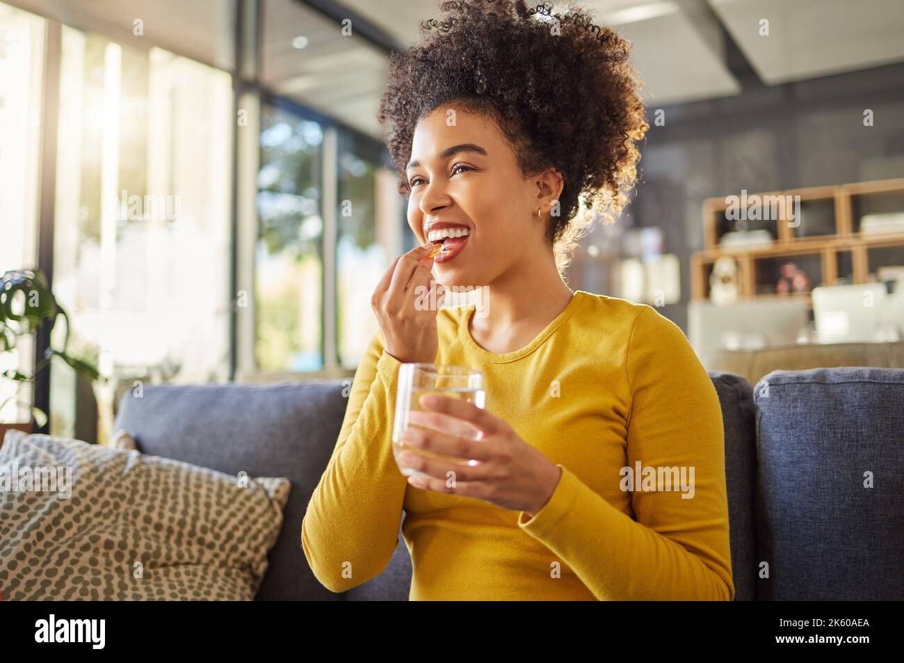 Young happy mixed race woman taking medication with water at home. One ...