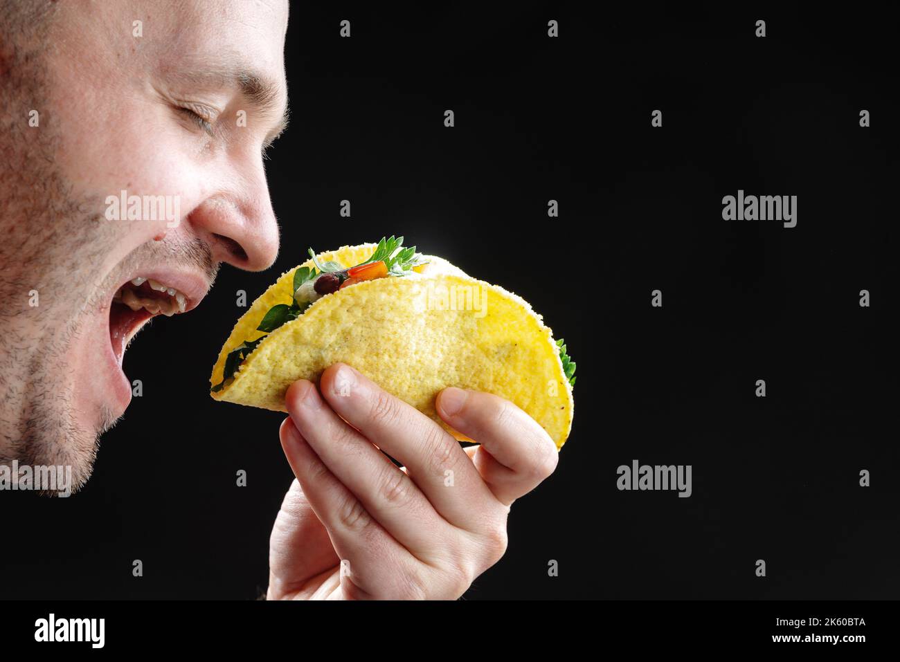 man eating tacos with vegetables on a black background. Blank space for ...