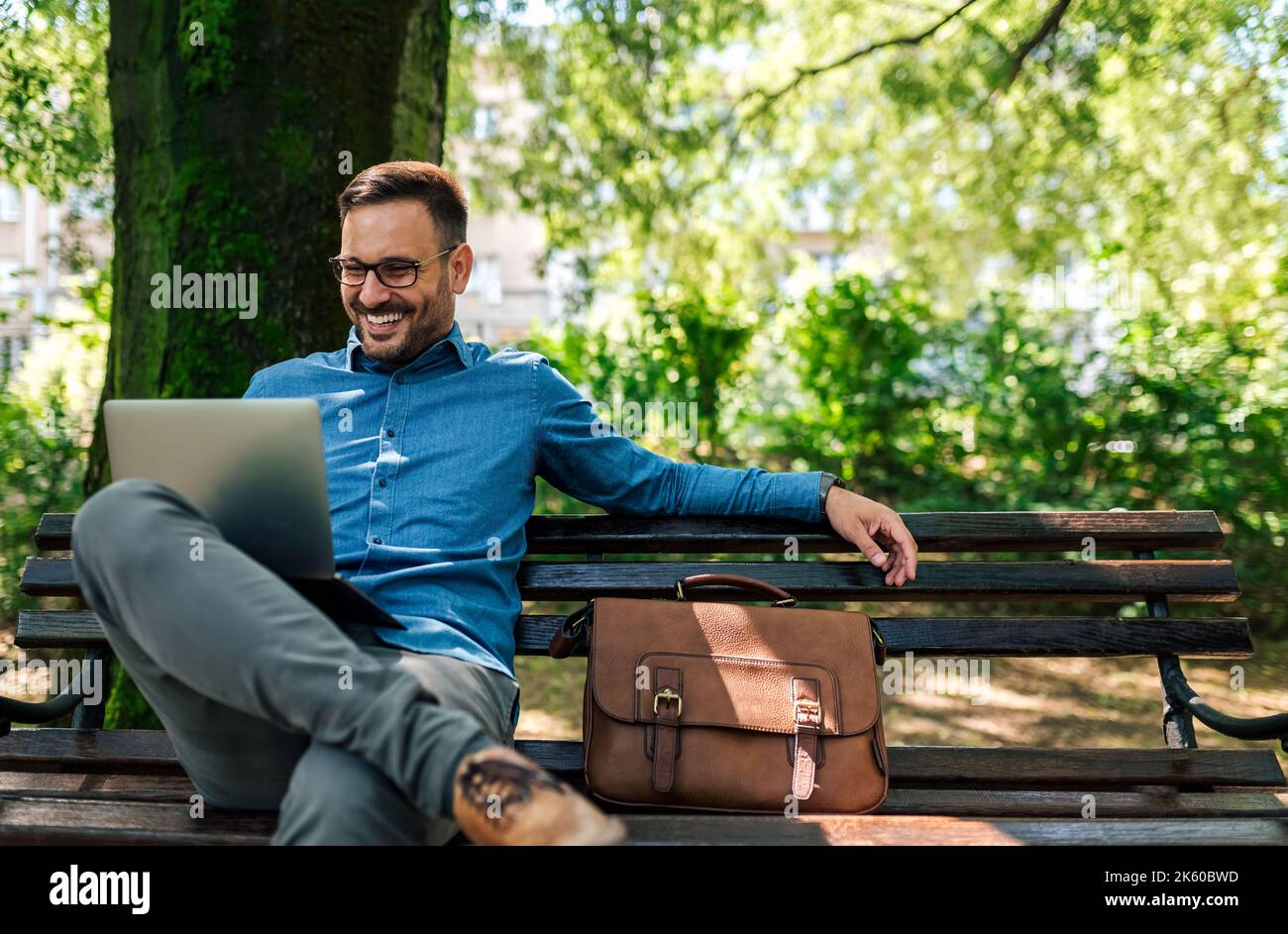 Casual young adult man, sitting cross-legged on the bench, resting his ...