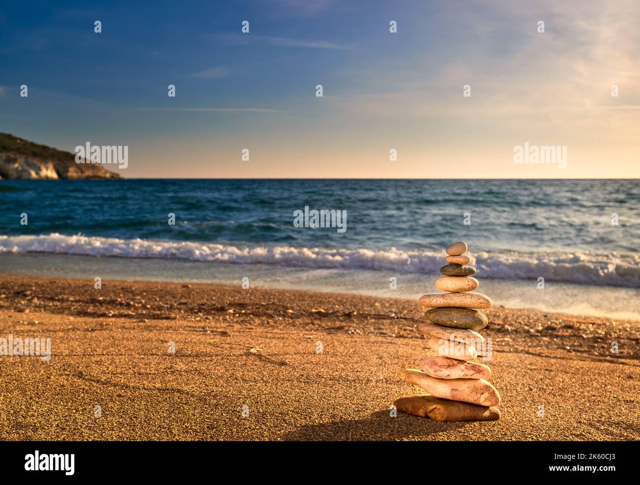 Balance stone stack on sandy beach in sunset sunlight, sea waves. Cairn ...