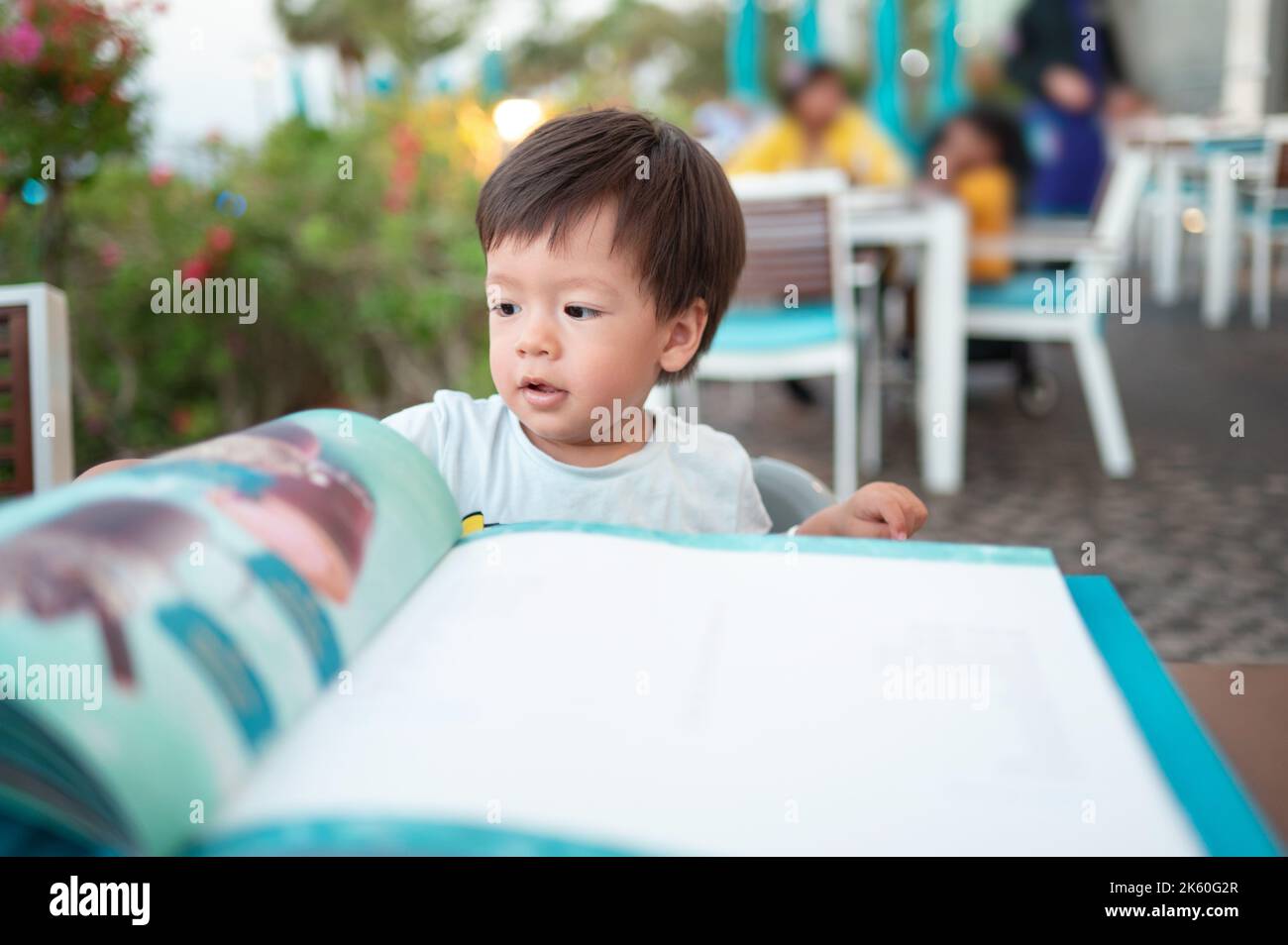 Handsome mixed race one year old baby boy looking at the menu to choose ...