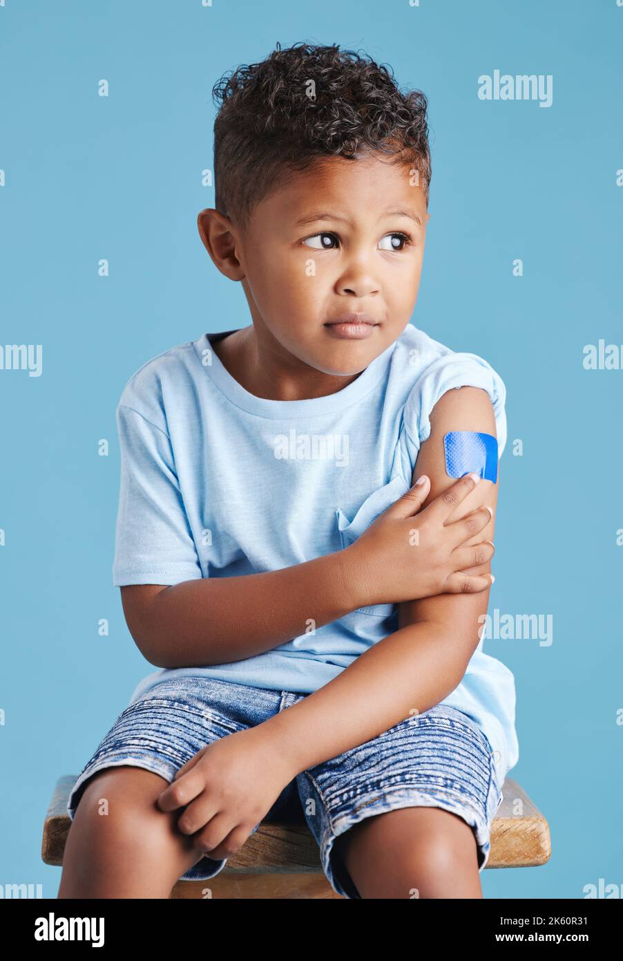 Vaccinated kid sitting on chair showing arm with adhesive bandage after ...