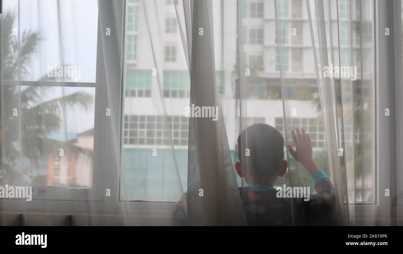a boy behind the curtain is looking at the beautiful view in the window ...