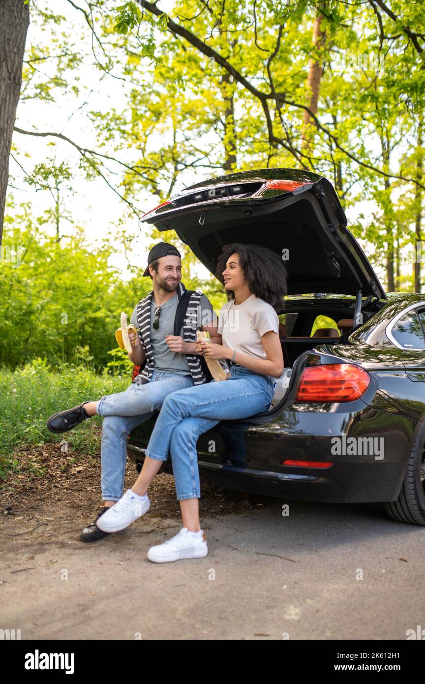 Young people sitting on the car boot and eating their lunch Stock Photo ...