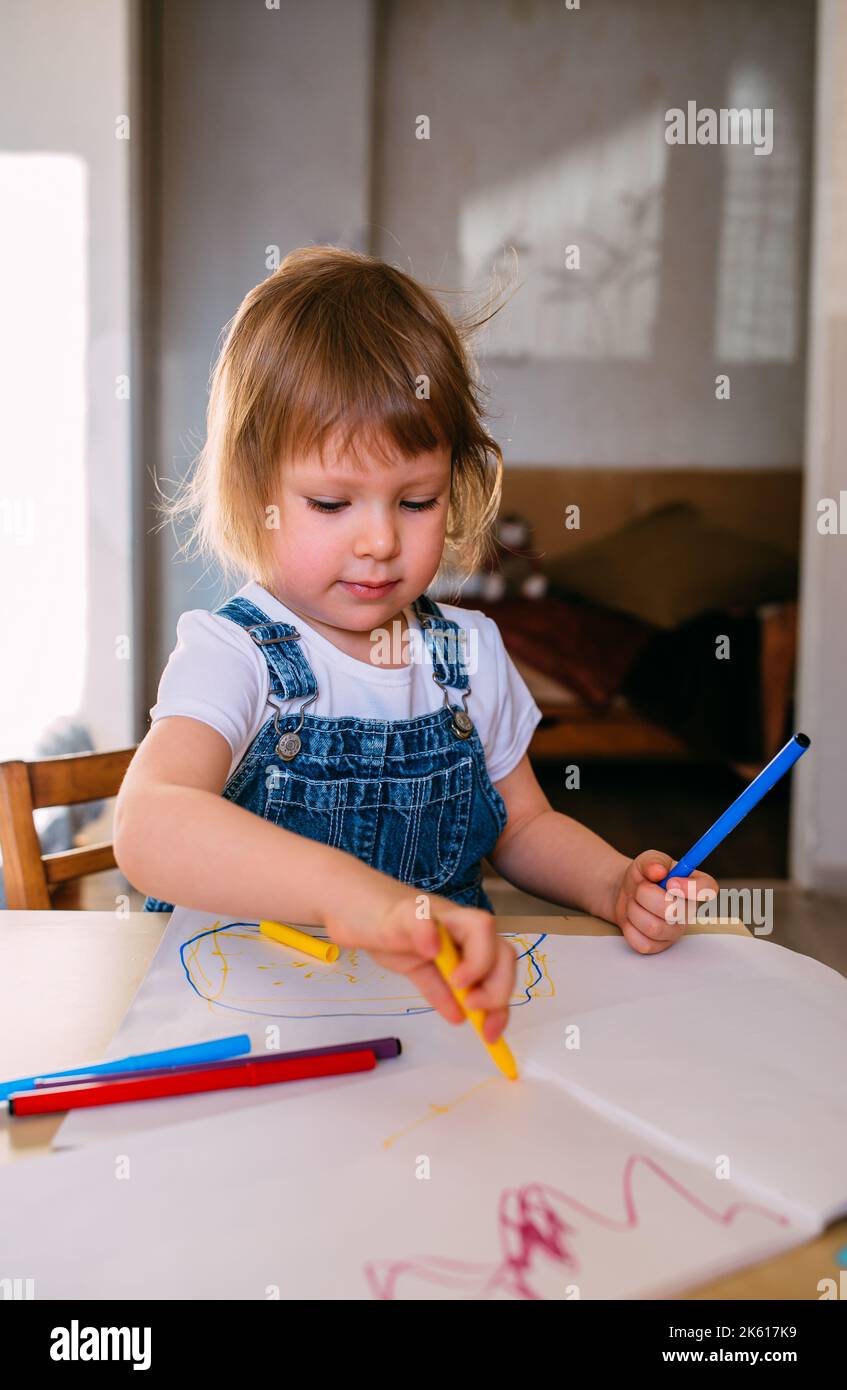 Small child at home at the children's table draws with felt-tip pens ...