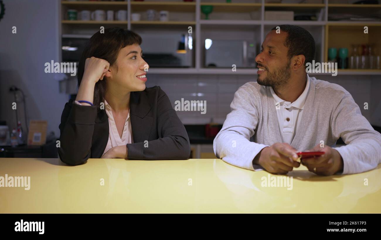 Two work colleagues in conversation at office kitchen table casually ...