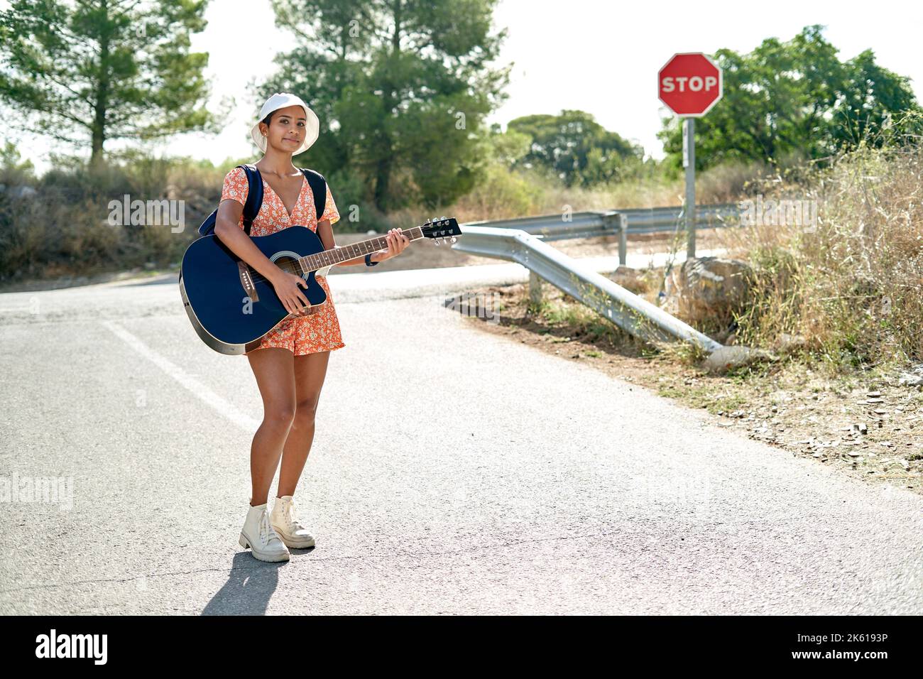 Full body of ethnic female musician in dress and hat playing guitar on ...