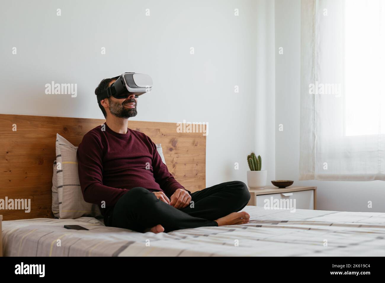 Man in VR headset sitting on bed with crossed legs in light cozy ...