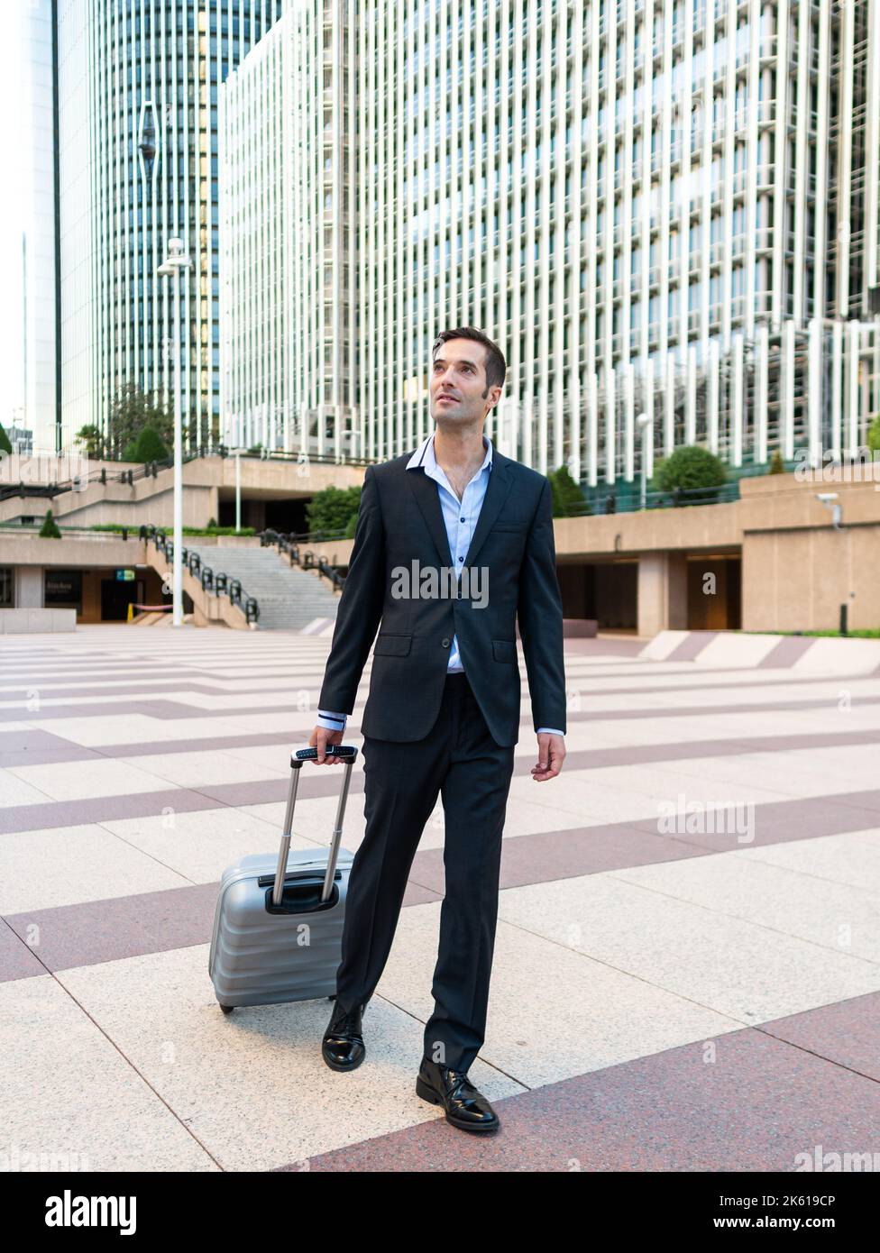 Full body of male in classy suit walking with suitcase and looking away ...