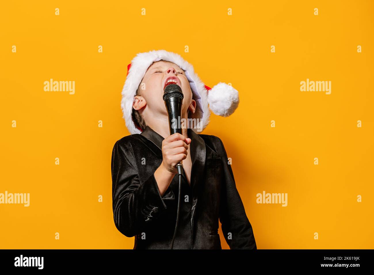 Boy in stylish jacket and Santa hat screaming loudly into microphone ...