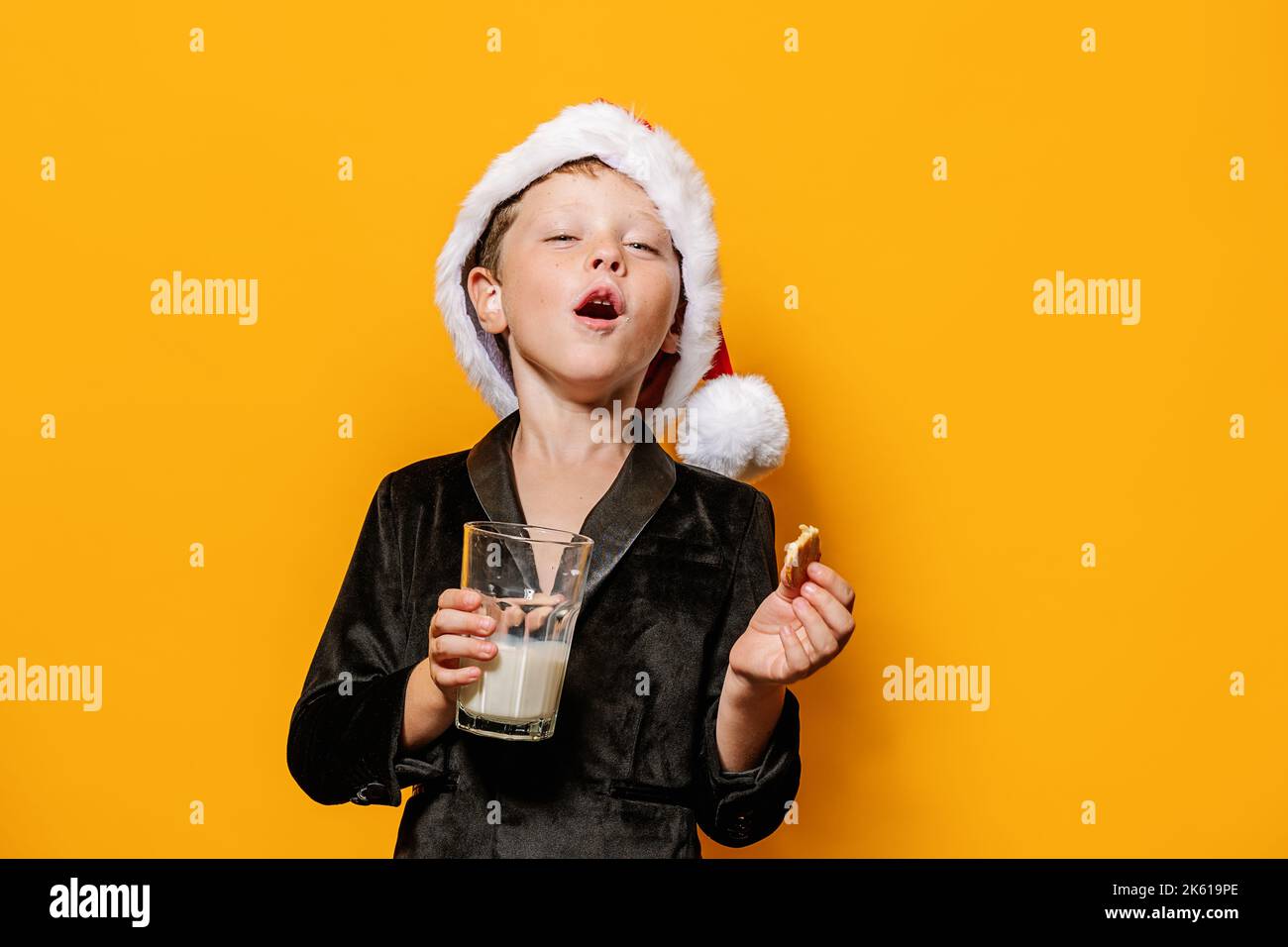 Funny boy in stylish black jacket and Santa hat looking at camera while ...