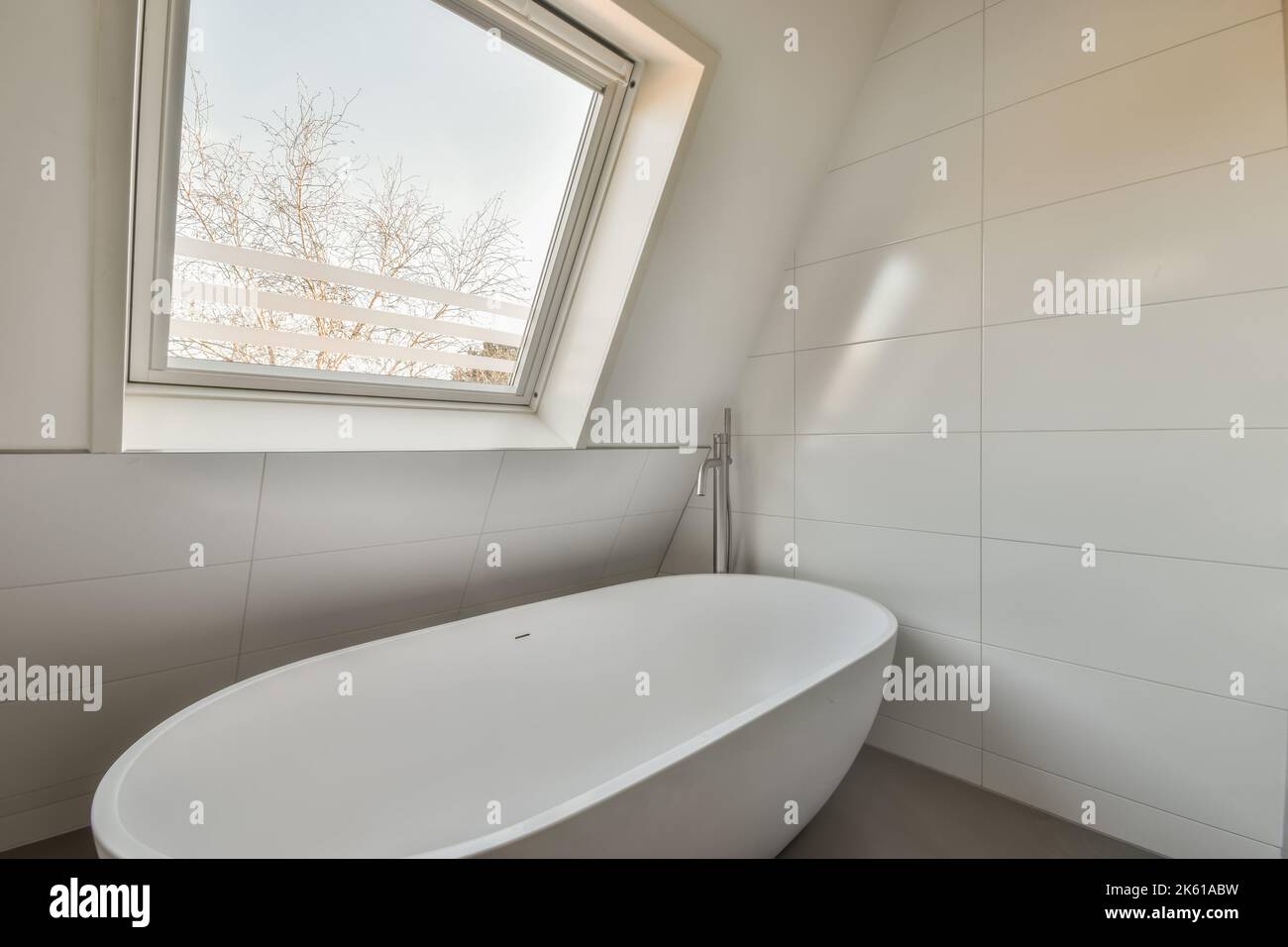 Bathtub below window in contemporary bathroom on sunny day in attic ...