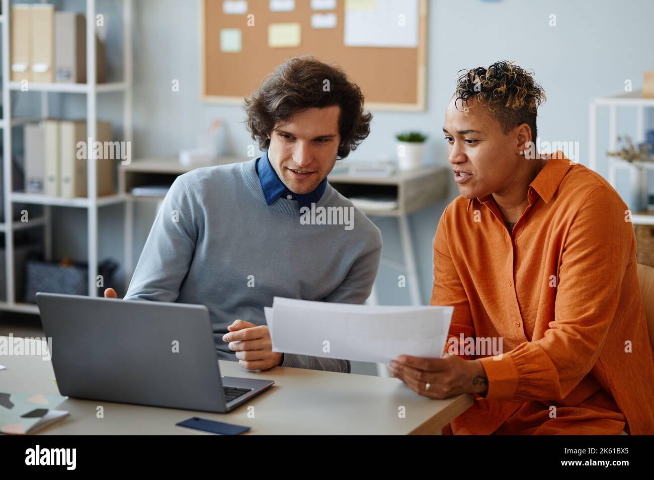 Portrait of two business people using laptop together while ...