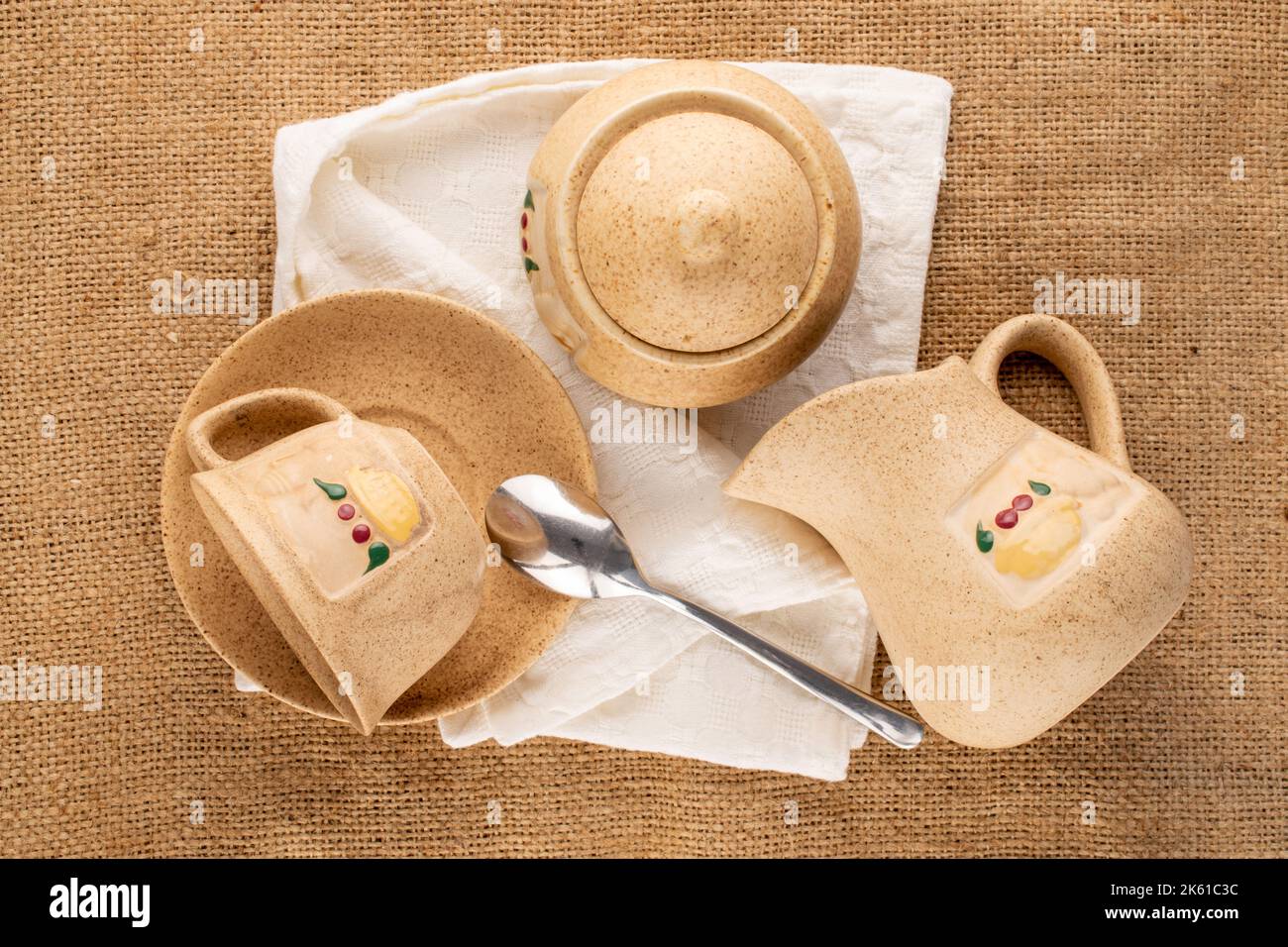 One clay cup on saucer, sugar bowl and milk jug with white linen napkin ...