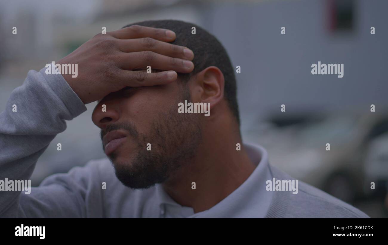 Frustrated young man feeling angst rubbing forehead with hand standing ...