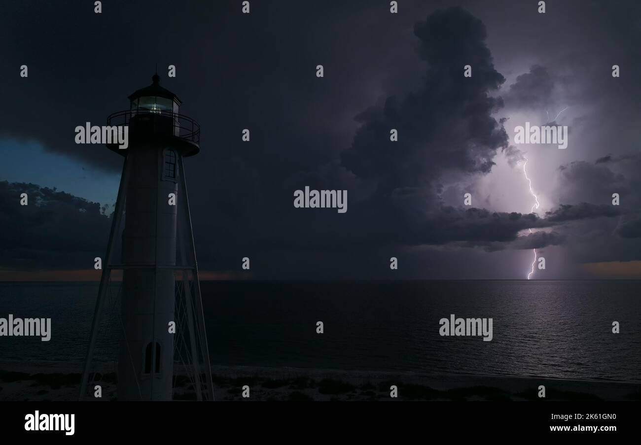 White tall lighthouse on sea shore with blinking light at stormy night ...