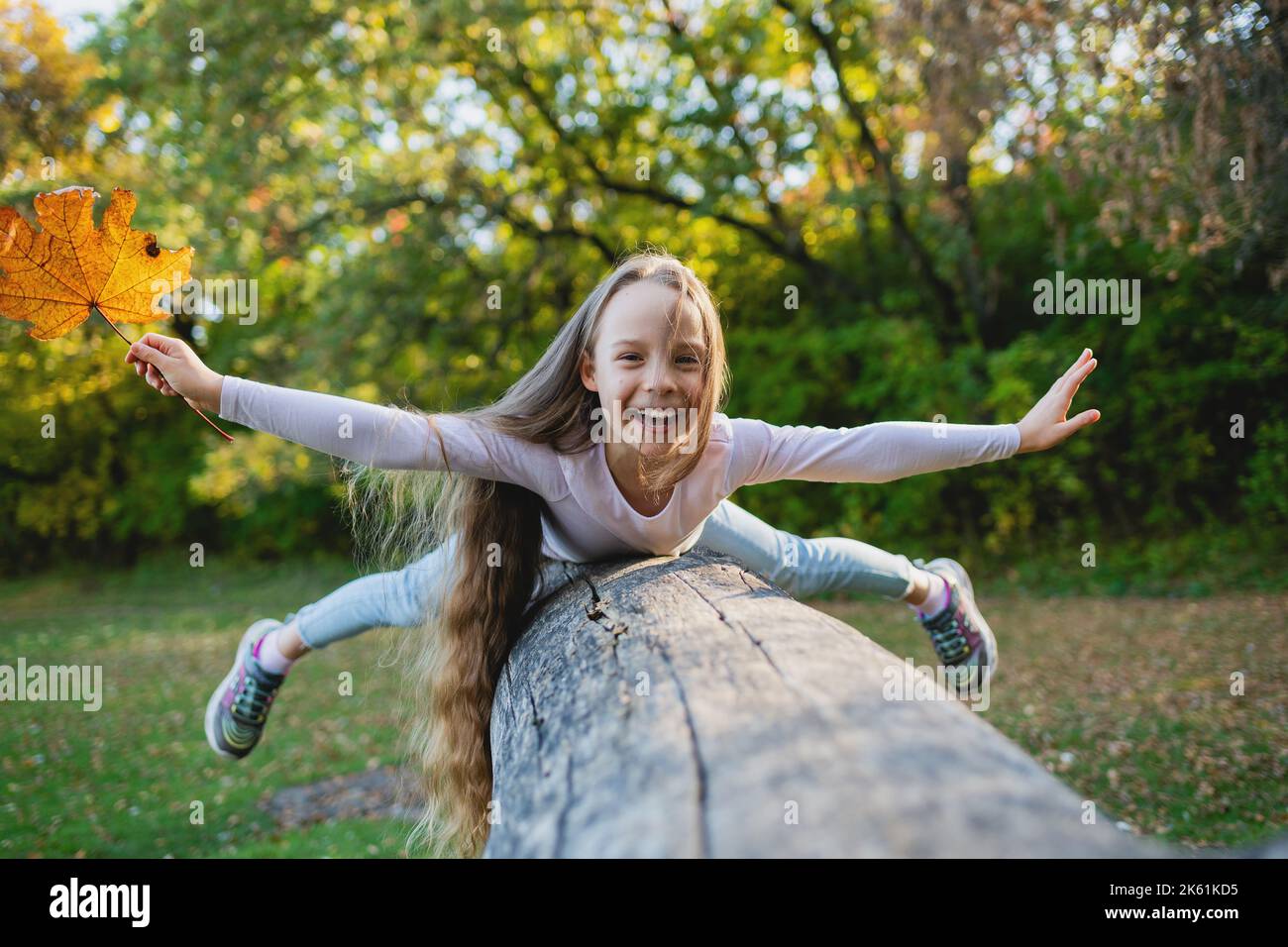 A cute girl lies on a fallen log in the park with her arms spread like ...