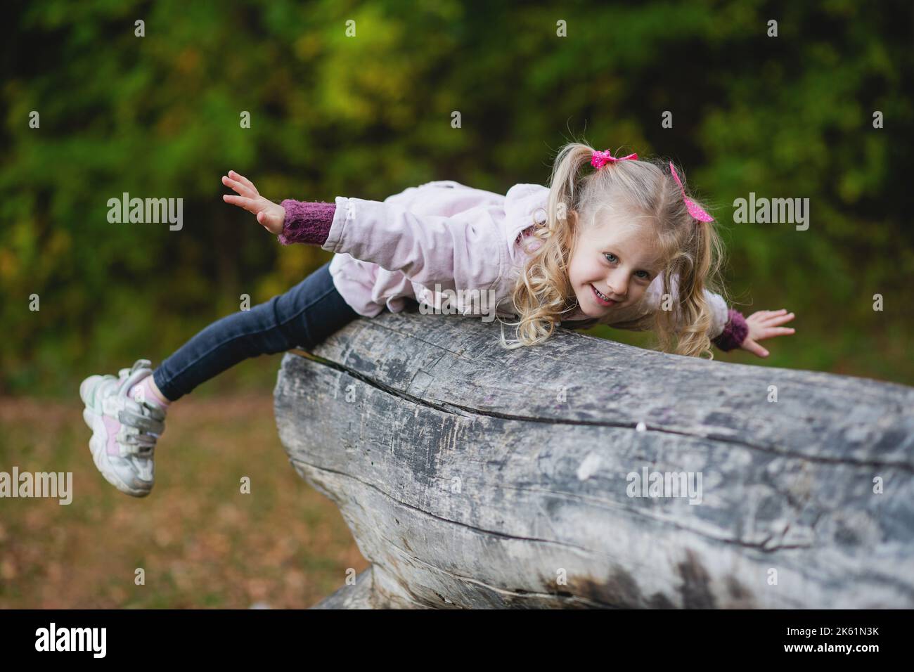 A cute girl lies on a fallen log in the park with her arms spread like ...