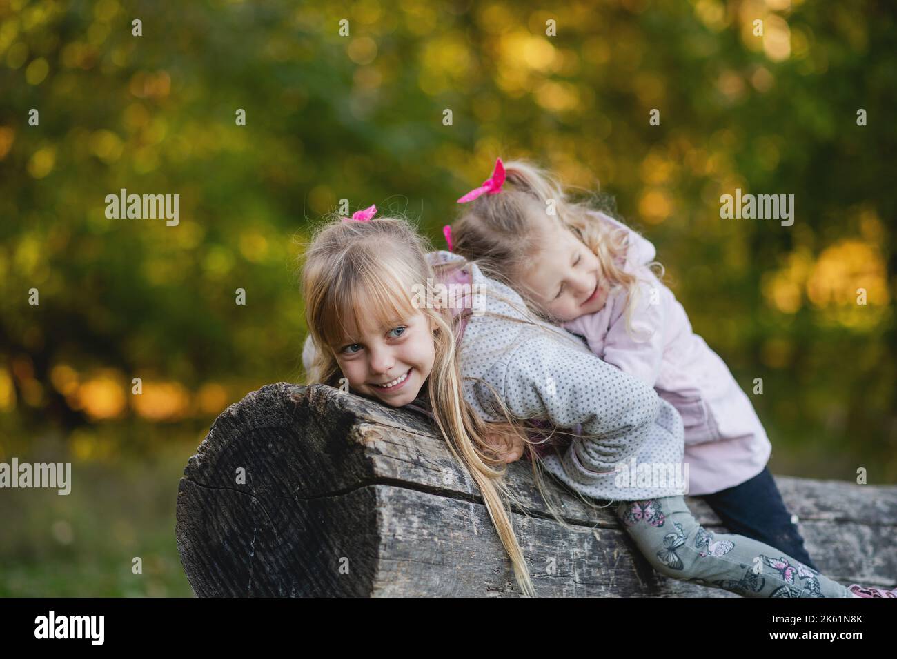 Two cute little girl lies on a fallen log in the park and smiles. Baby ...
