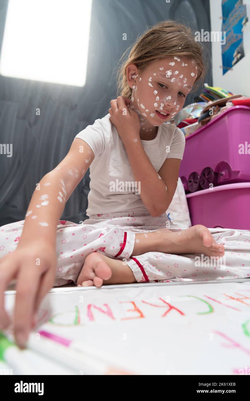Little school girl with chickenpox drawing on white board in kids' room ...