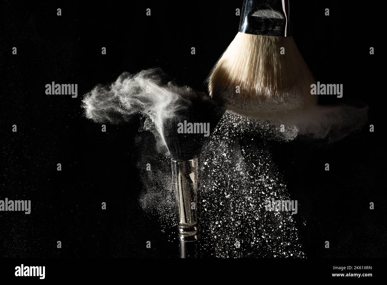 Two brushes touching, spilling powder over a black background Stock ...