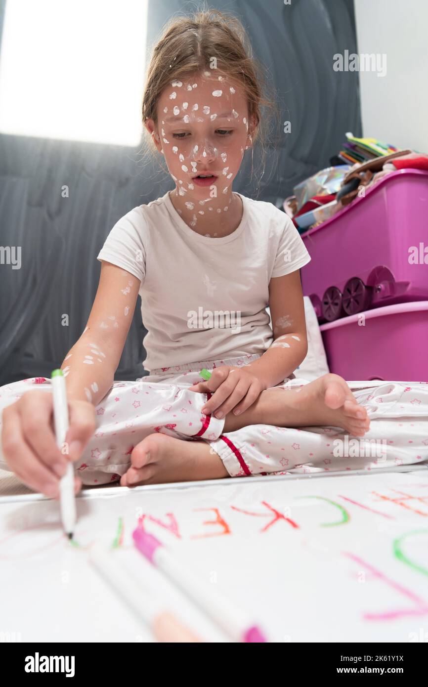 Little school girl with chickenpox drawing on white board in kids' room ...