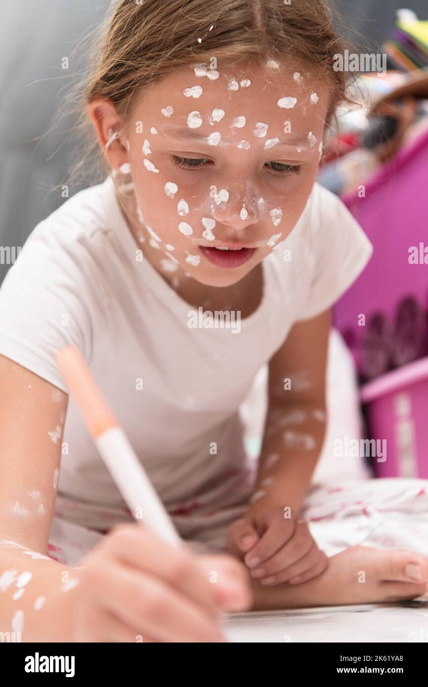 Little school girl with chickenpox drawing on white board in kids' room ...