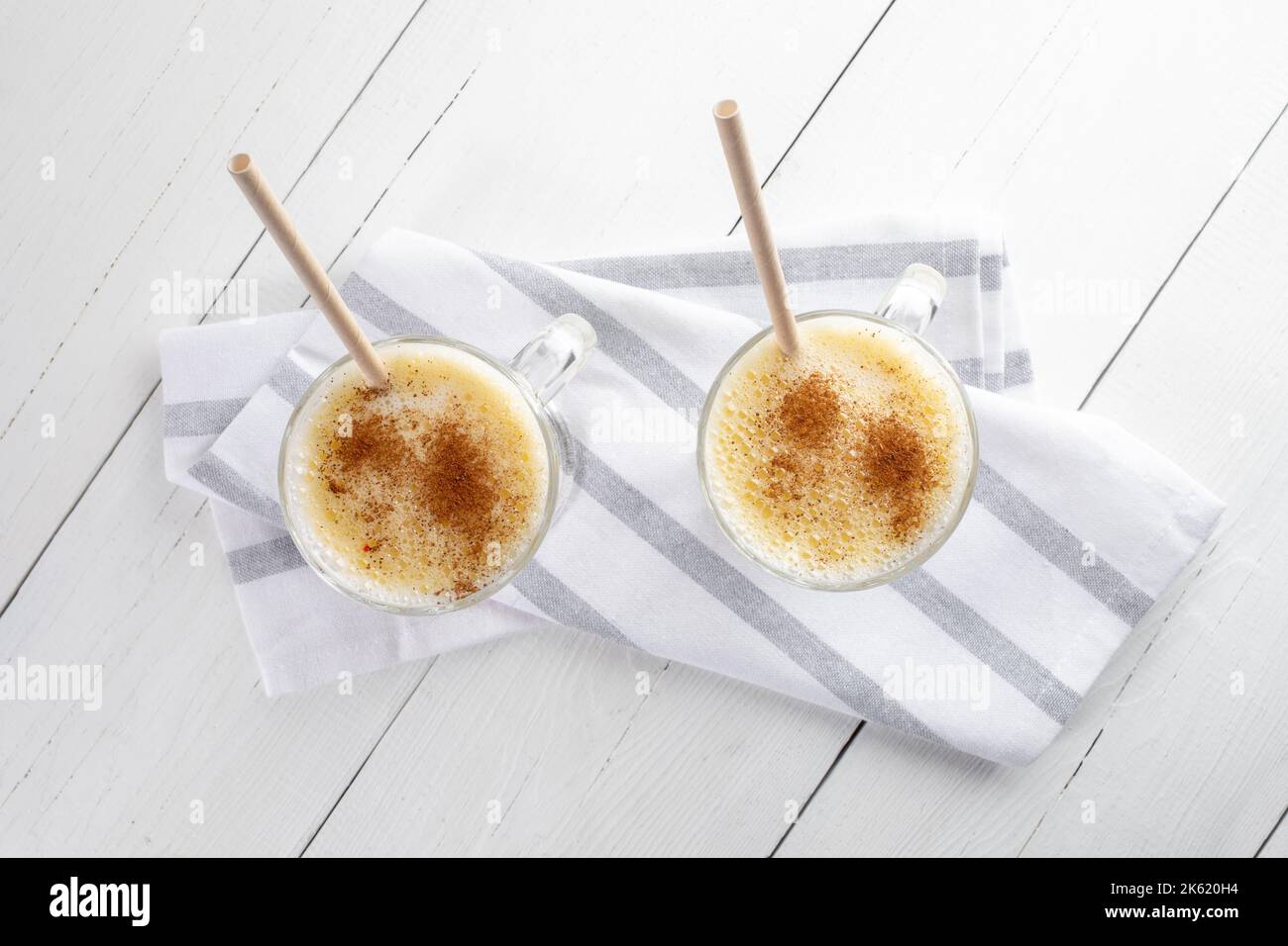 Two glasses of homemade eggnog with cinnamon and paper drinking straws ...