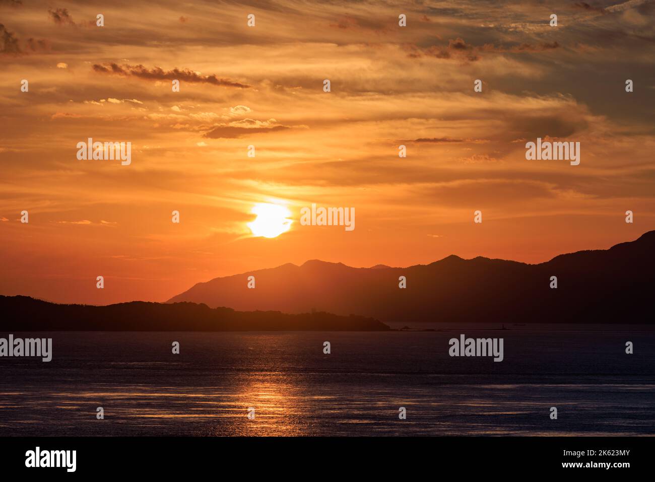 Low sun behind clouds at horizon over distant silhouetted mountains ...