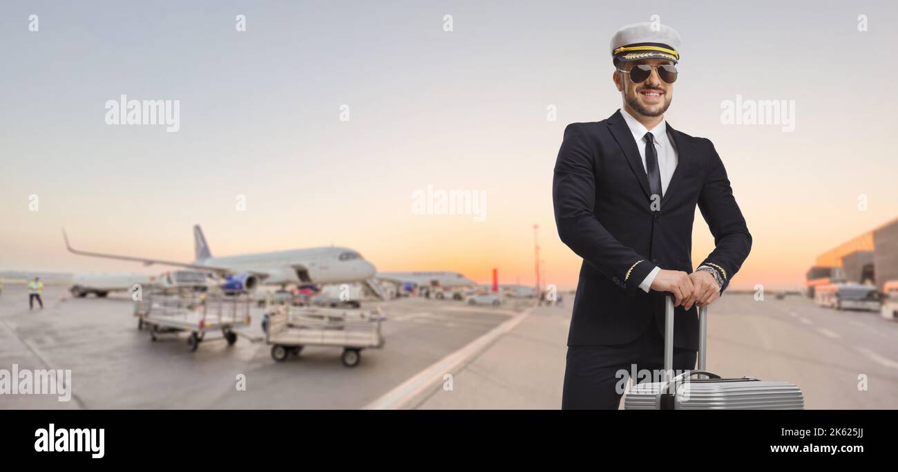 Pilot with a suitcase posing on an airport with plane in the background ...