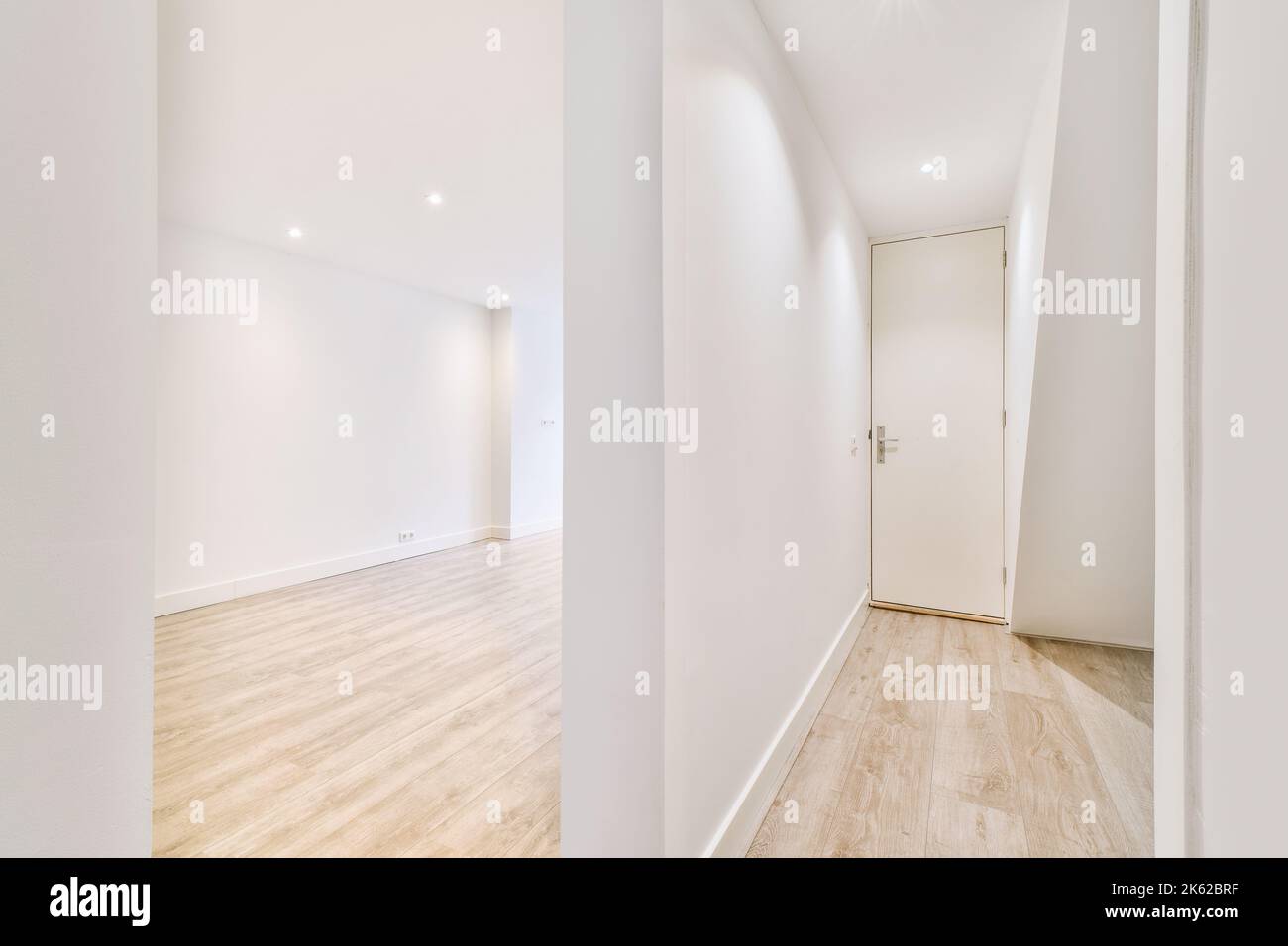 Narrow corridor with white walls and doors leading to spacious room ...