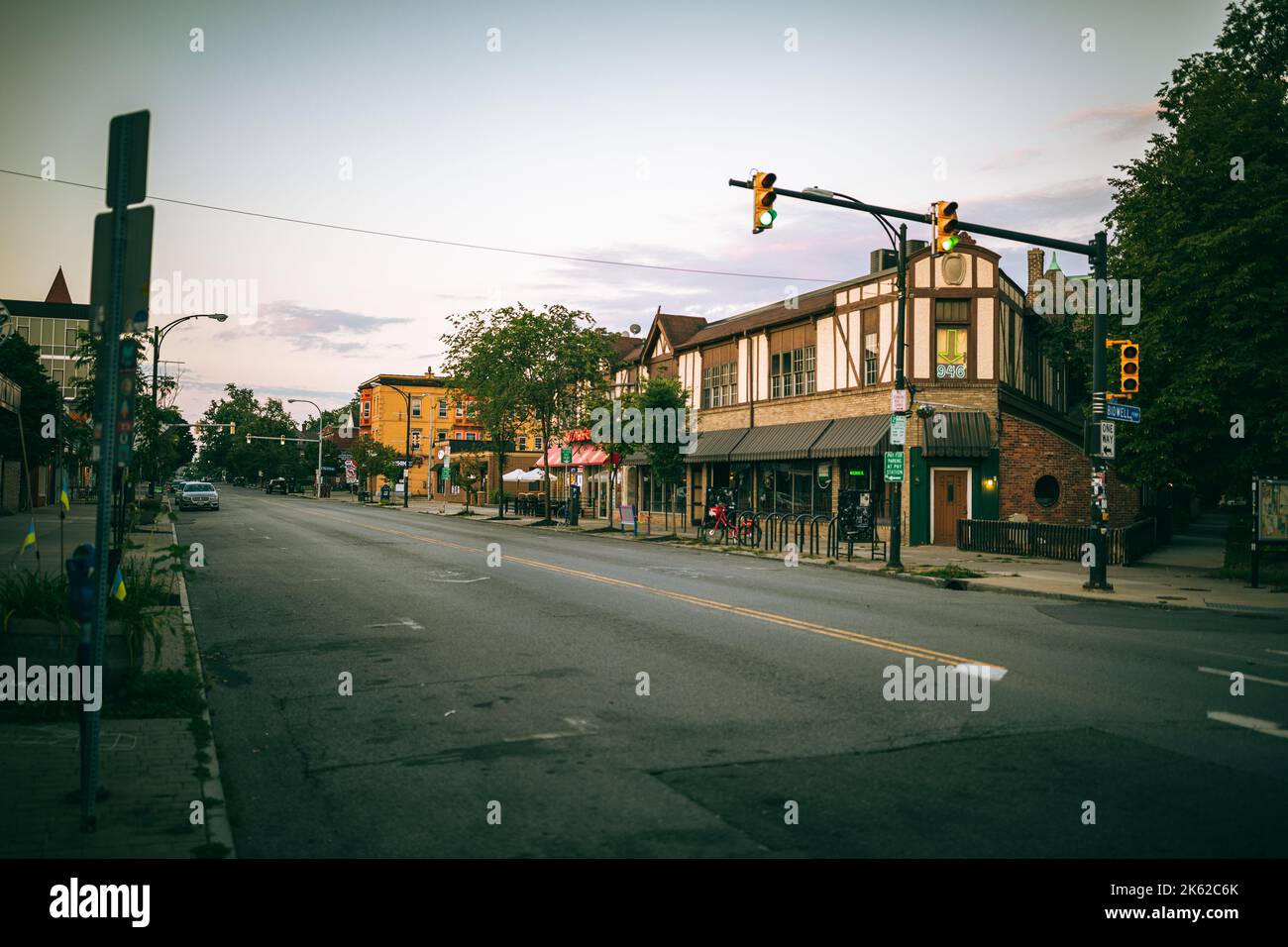 The view of a wide street with trees and buildings under the bright sky ...