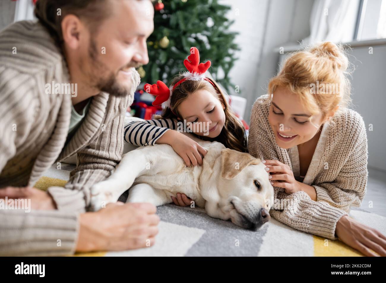 Positive mother and daughter petting labrador near blurred father at ...