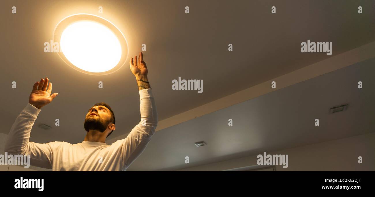A young man stands on a stepladder and installs a large chandelier on ...