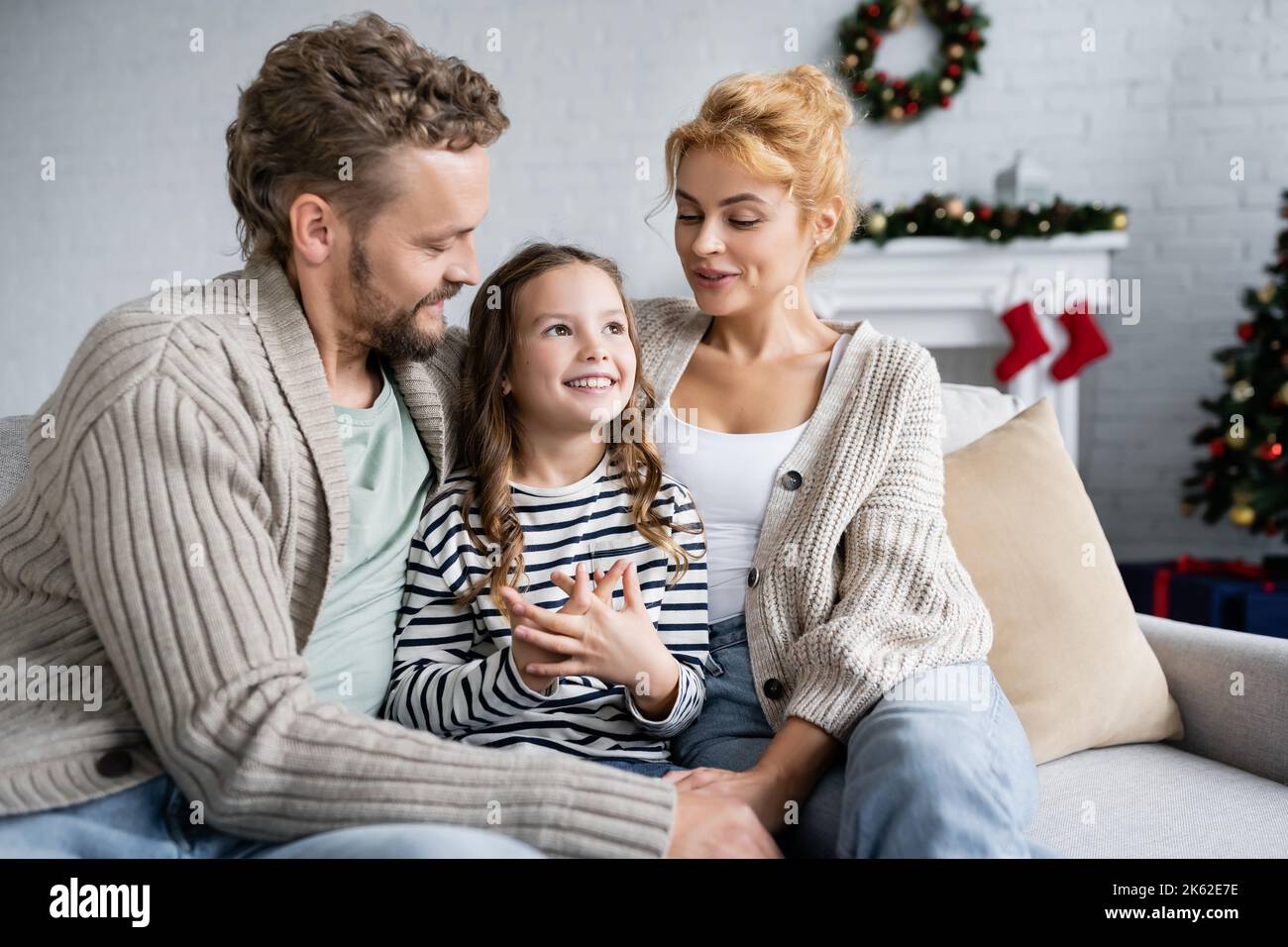 Pleased kid sitting near parents on couch during christmas at home ...