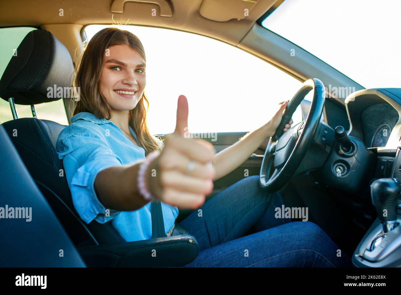 Beautiful happy woman driving her new car and showing thumbs up gesture ...