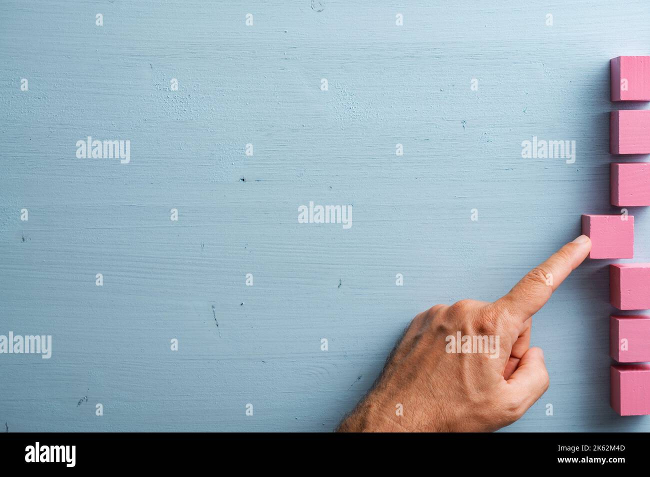 Male hand pushing a pink wooden block into a stack of them on the right ...