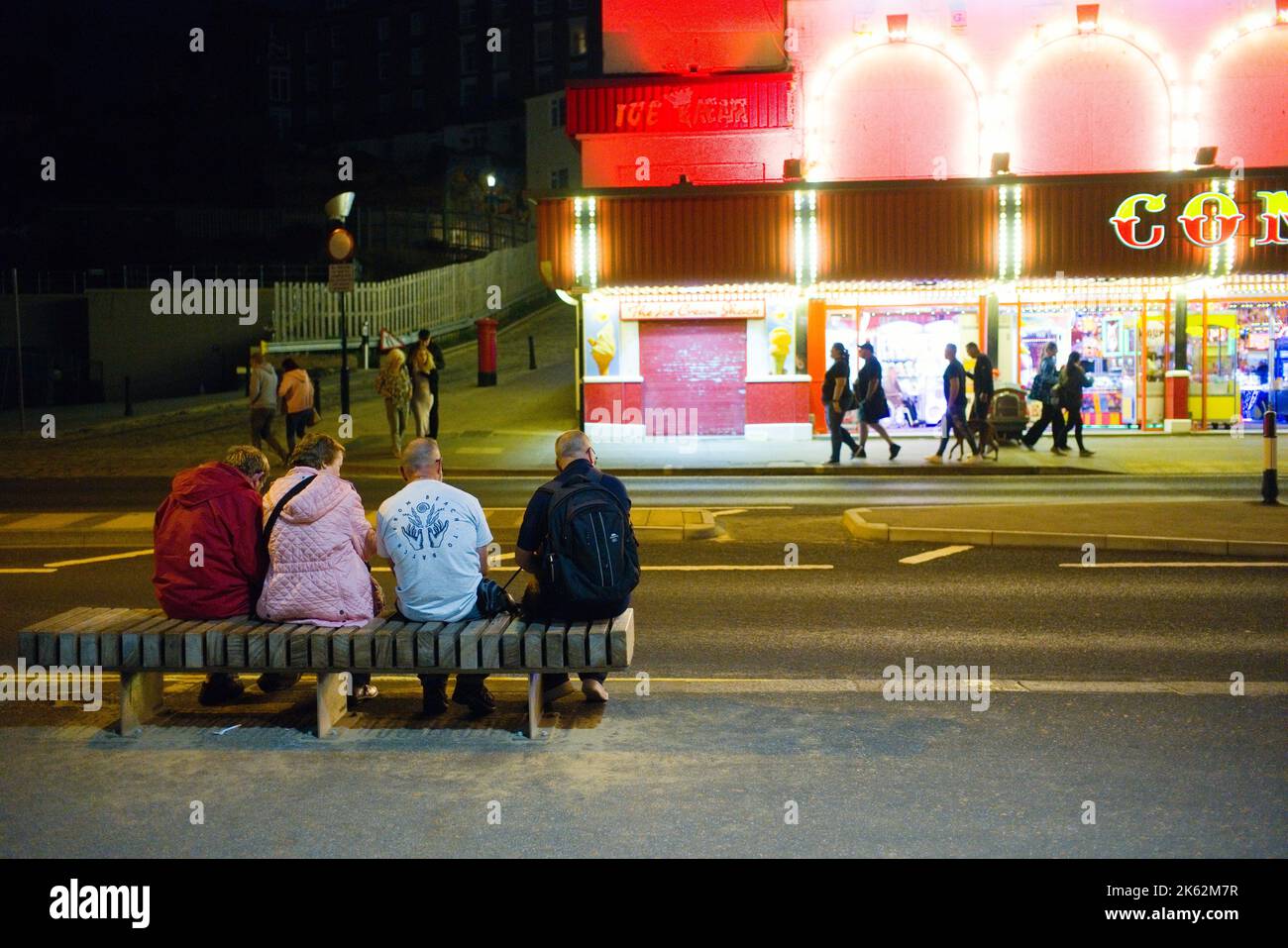 Four visitors to Scarborough sitting on a seafront bench at night Stock ...