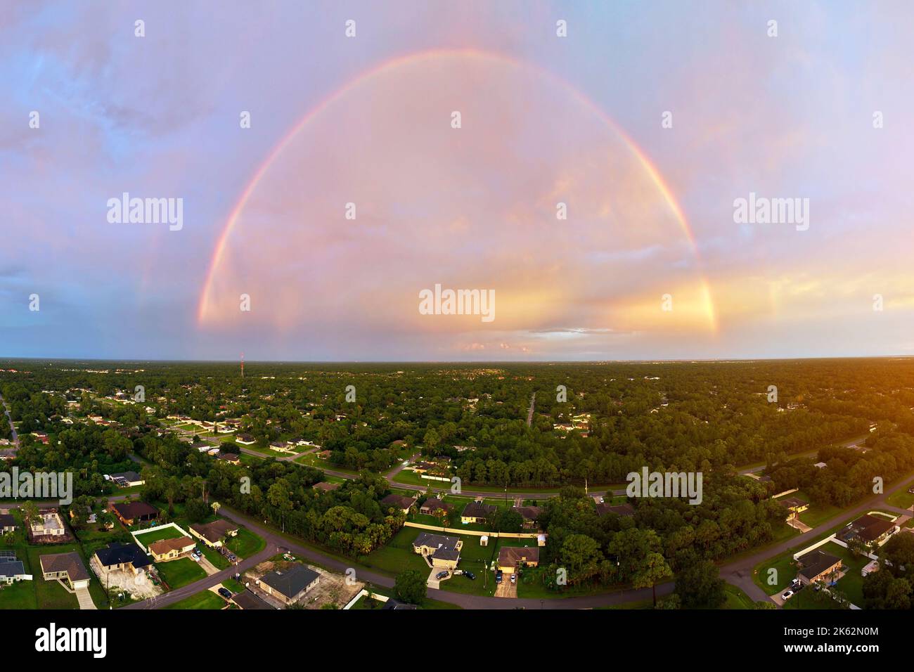 Colorful round rainbow over rural town suburbs against blue evening sky ...