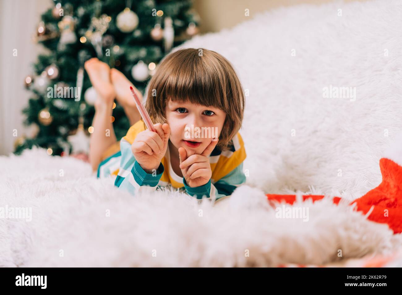 Smiling Kid boy lying on couch and writing the letter to dear Santa at ...