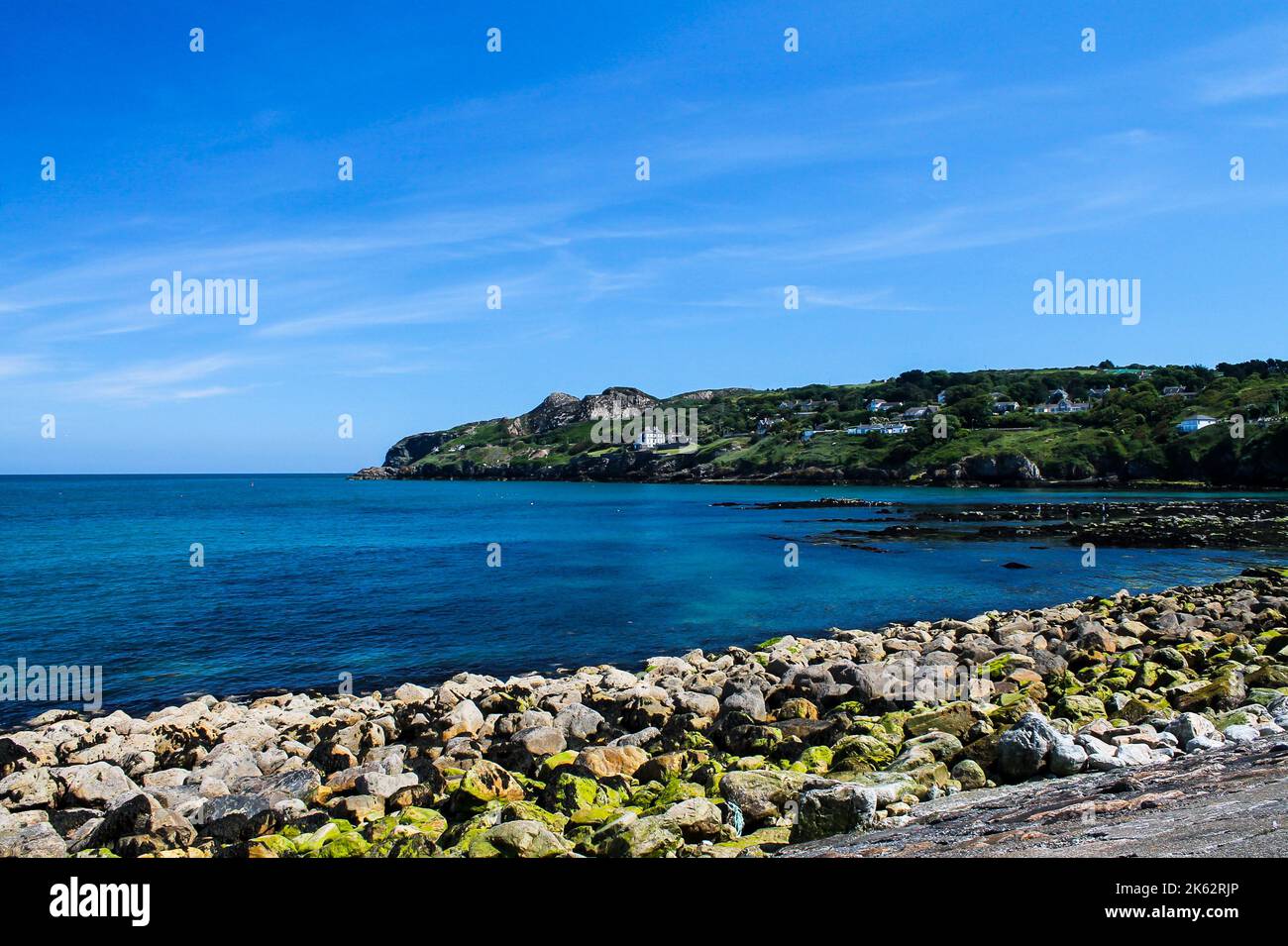 A closeup of Howth Dublin rocky beach with the blue clear sea and sky ...