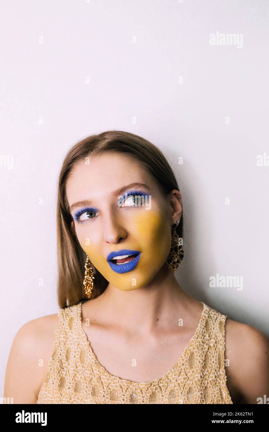 Portrait of pretty blonde girl with extreme, blue-yellow make-up; she ...