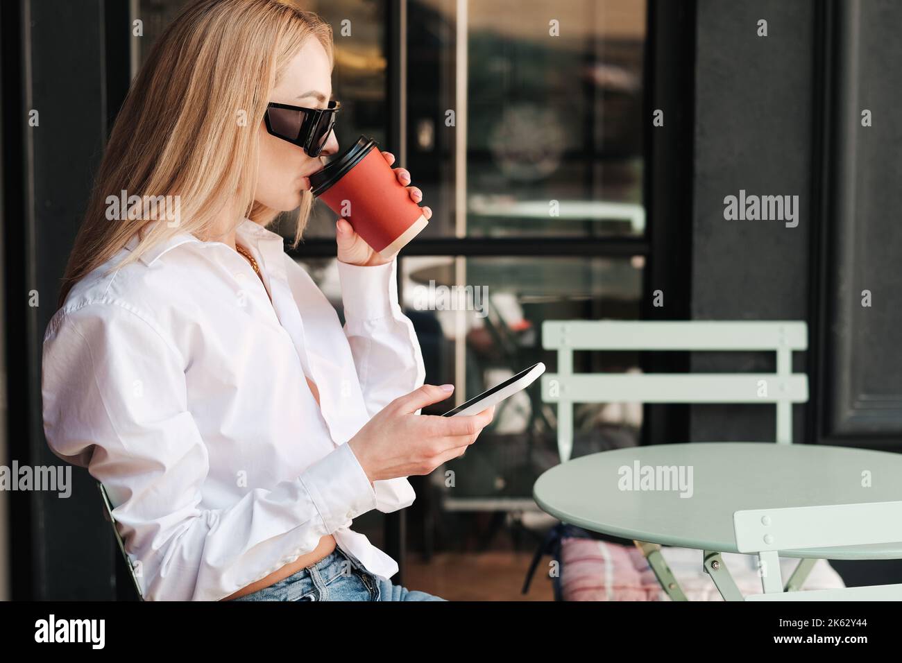 Elegant Woman Sitting at a Cafe Table and Drinking While Using ...