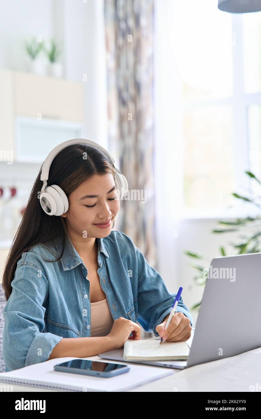 Teen asian student making notes in notebook during online lesson ...