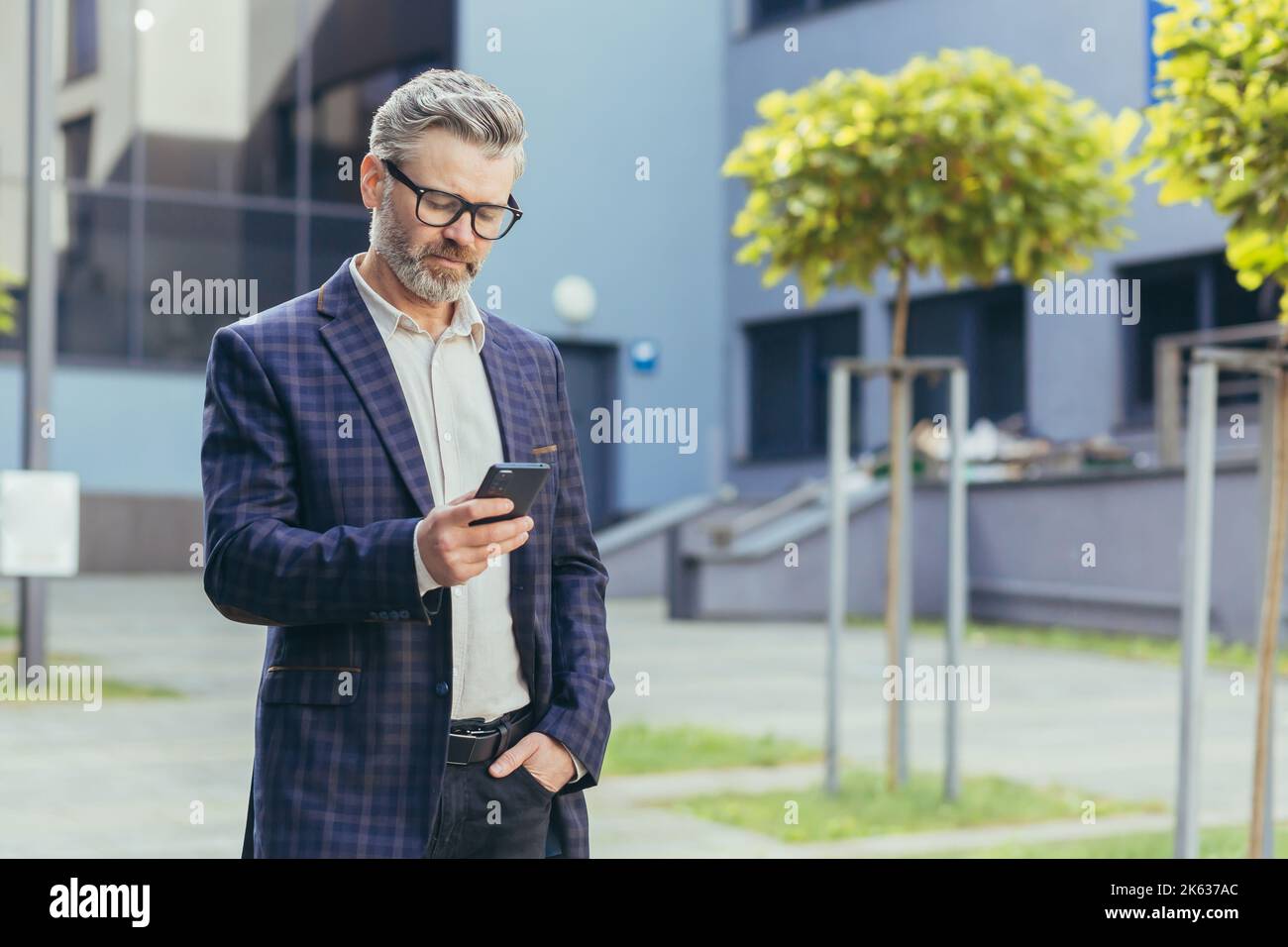 Serious and focused mature businessman using smartphone outside office ...