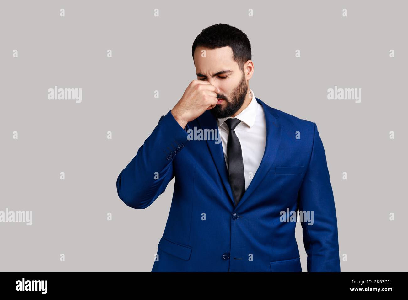 Portrait of bearded man grimacing with disgust, holding breath, pinching nose with fingers to ...